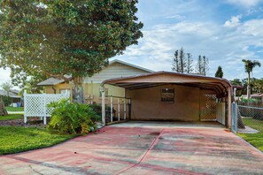 Garagem residencial com acesso coberto, cerca branca e uma árvore ao fundo.