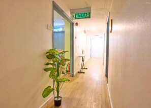 Um corredor com um vaso de planta, uma placa indicando direção e uma porta no final.