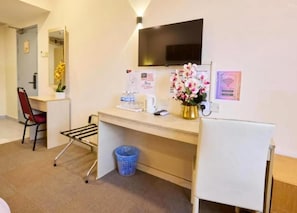 Quarto de hotel com escrivaninha, cadeira e televisão fixada na parede.