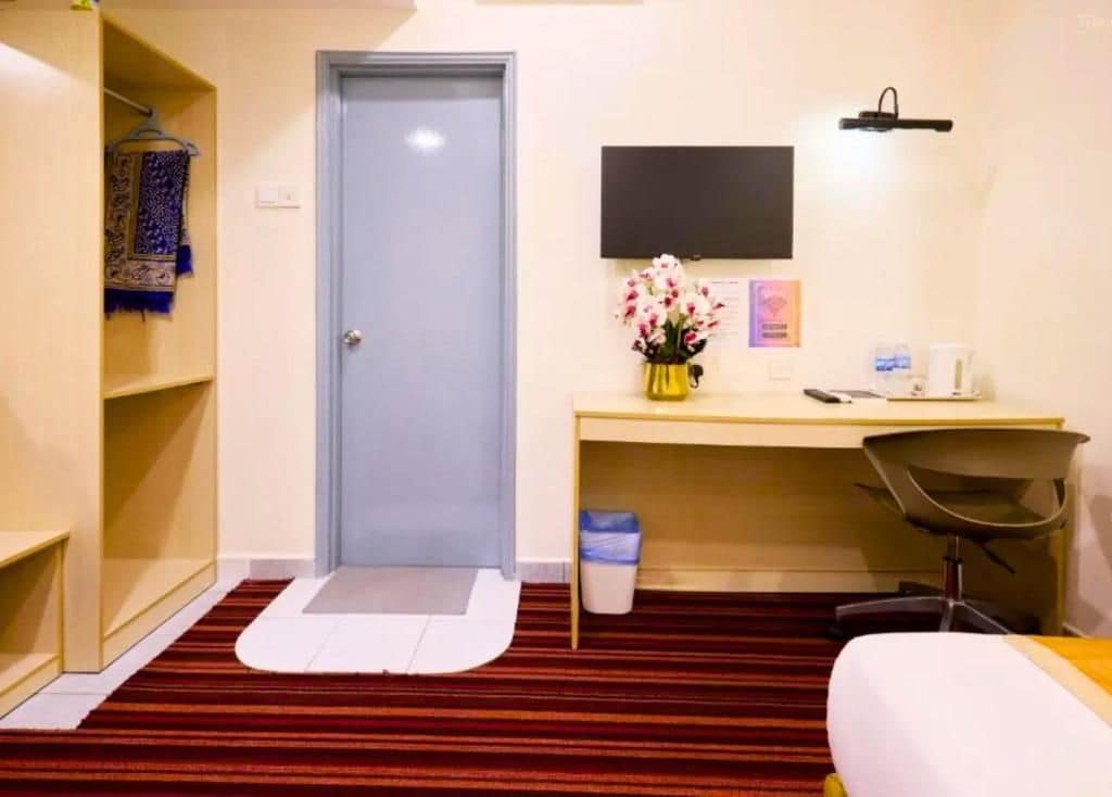 Quarto de hotel com uma cama, uma escrivaninha com cadeira, uma televisão e uma porta.