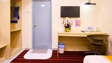 Quarto de hotel com uma cama, uma escrivaninha com cadeira, uma televisão e uma porta.