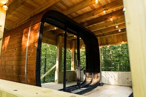 Uma cabana de madeira com entrada arqueada, um deck de madeira e vista para a floresta ao redor.