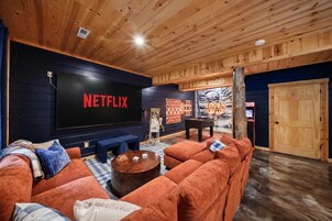 Uma sala de estar acolhedora com uma grande TV de tela plana, uma mesa de futebol e um sofá confortável.