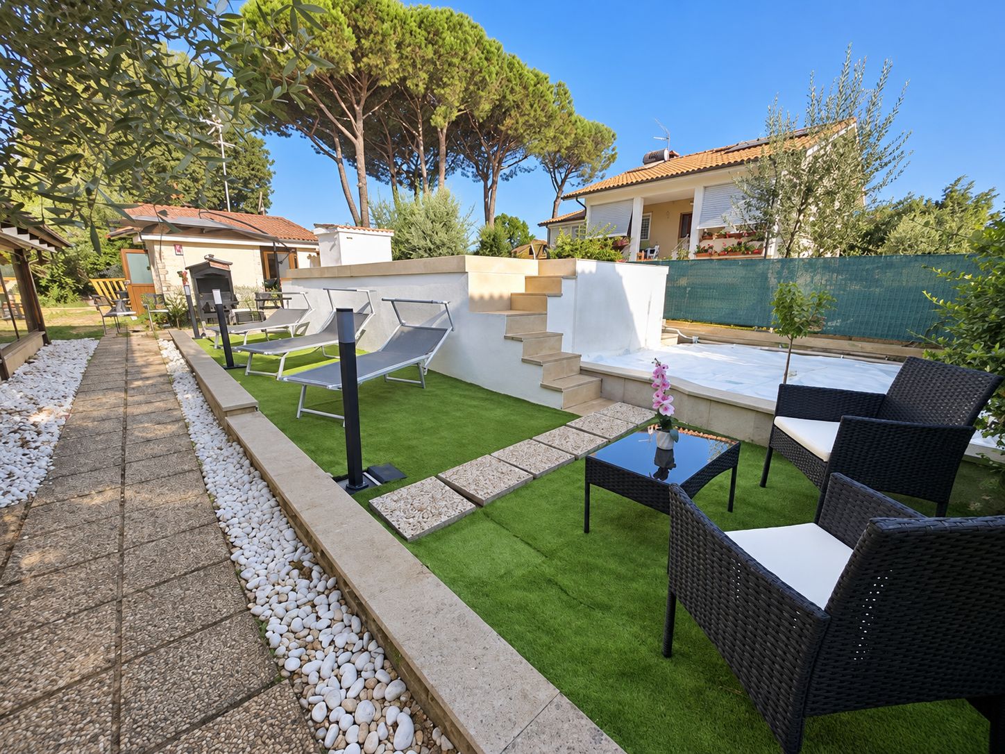 Área de pátio com mobiliário externo, uma piscina pequena e uma escadaria que leva a um deck coberto.
