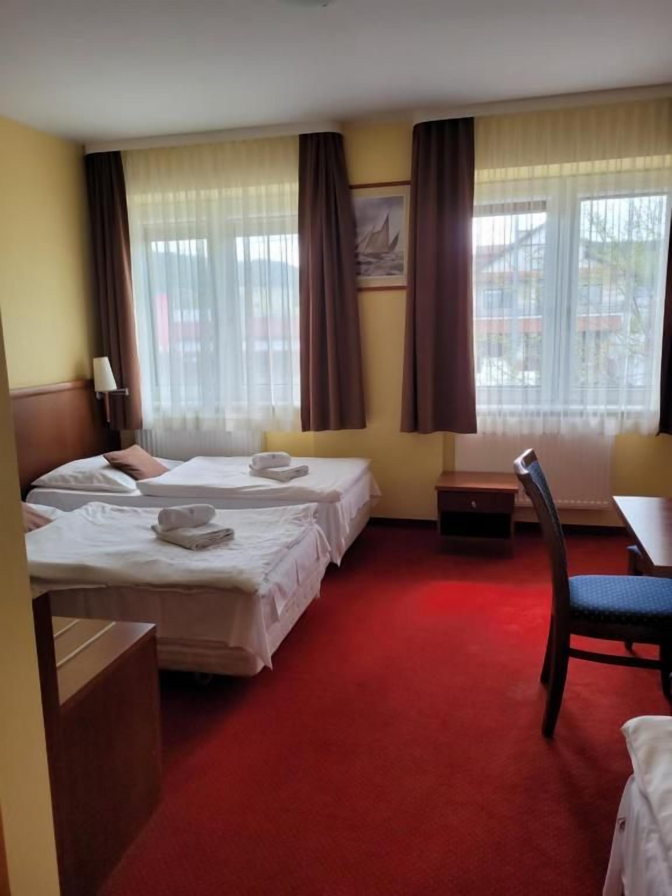 Quarto de hotel com duas camas, uma escrivaninha, uma cadeira e uma janela com cortinas.