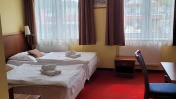 Quarto de hotel com duas camas, uma escrivaninha, uma cadeira e uma janela com cortinas.