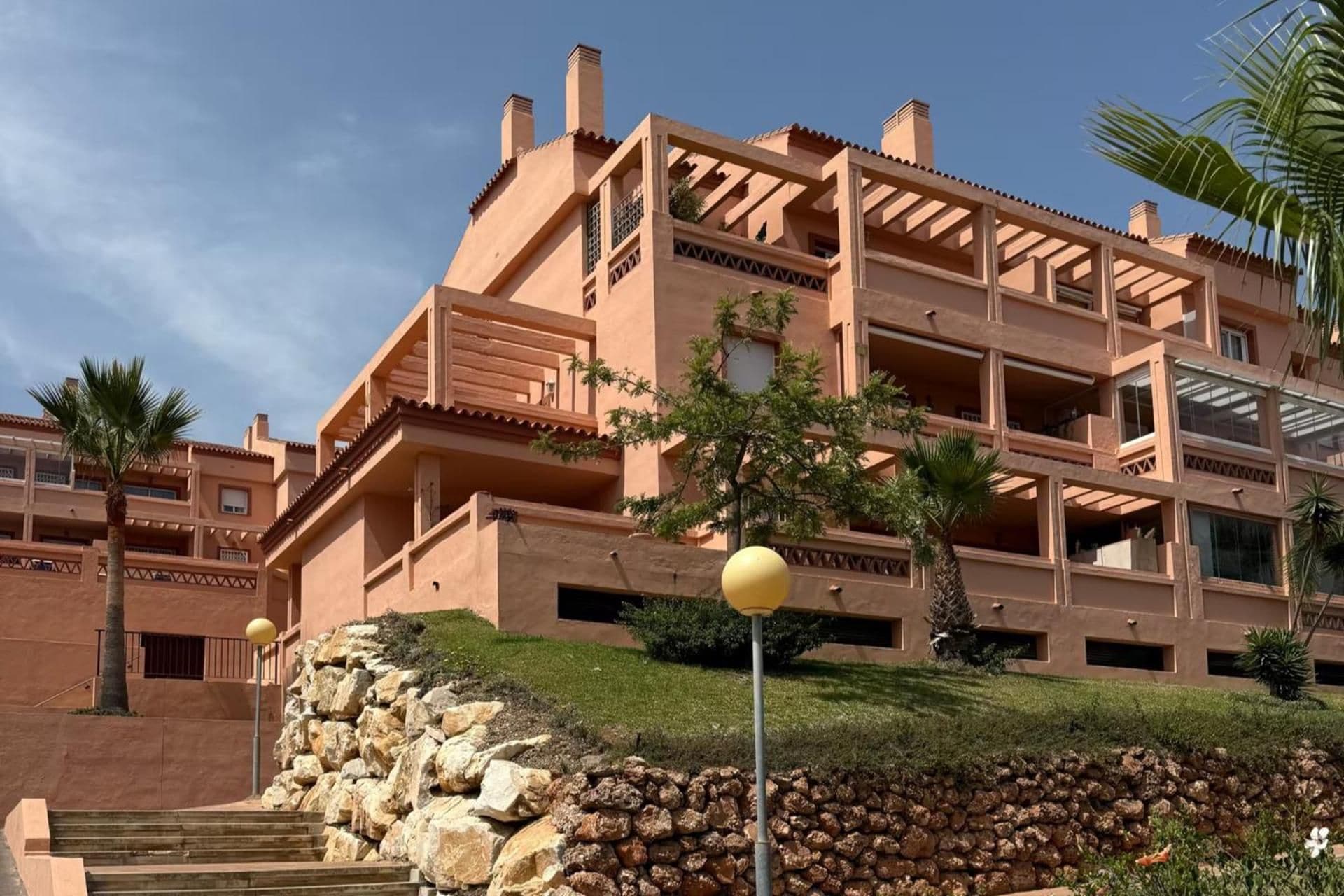 Um edifício com vários andares, varandas, uma parede de suporte de pedra e céu claro.