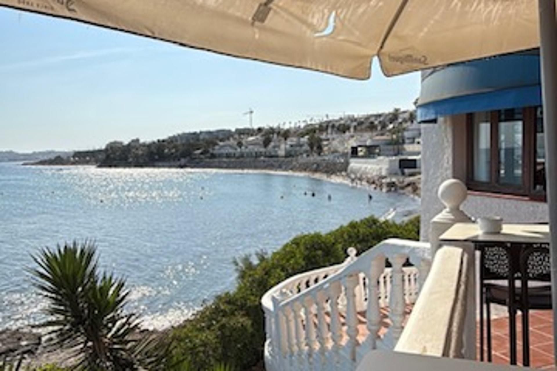 Um imóvel à beira-mar com varanda e vista para o oceano, corrimão branco e panorama da costa.