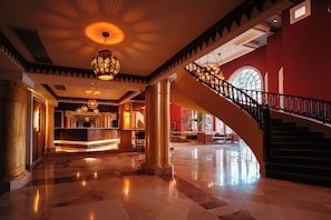 Um hall espaçoso com uma escadaria imponente, piso de mármore e luminárias decorativas.
