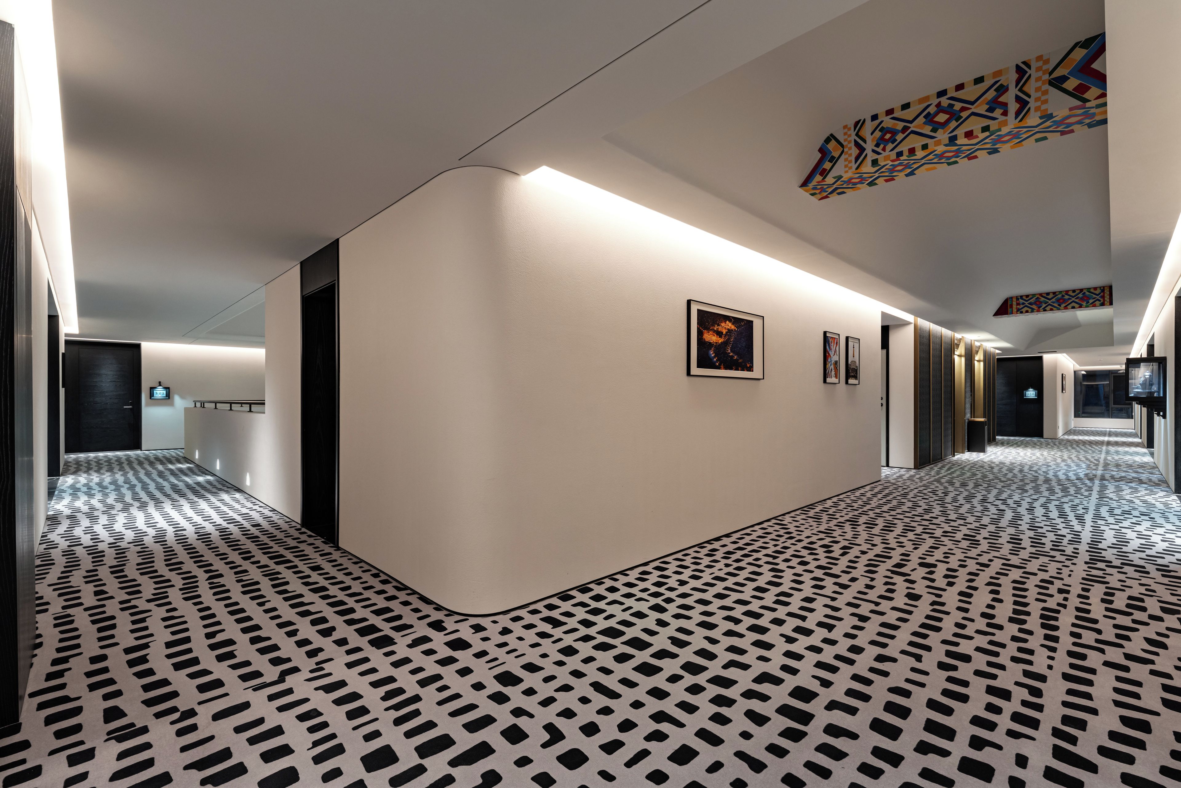Um corredor com piso estampado, parede curva e teto com iluminação embutida.