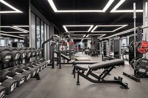 Uma academia com equipamentos de musculação, bancos e um espelho grande na parede.