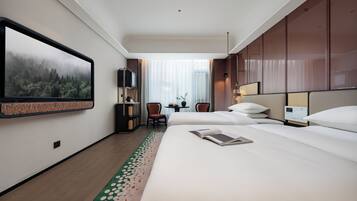 Quarto de hotel com uma cama grande, escrivaninha, cadeira, televisão e vista para uma floresta pela janela.