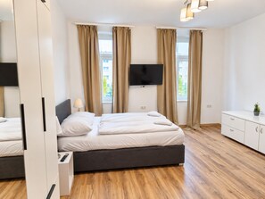 Quarto de hotel com cama, televisão, mesa de cabeceira, cômoda e janela com cortinas.