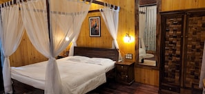 Uma cama com dossel e colunas, cabeceira de madeira, mesa de cabeceira com abajur e um espelho.