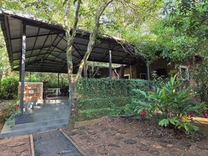 Área externa coberta com um banco de pedra, uma mesa pequena e um vaso de planta.
