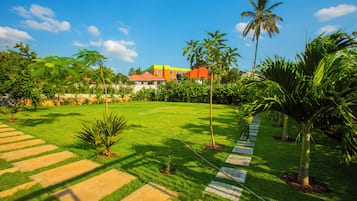 Um jardim bem cuidado, com gramado, palmeiras e um caminho que leva a um edifício com telhado vermelho.
