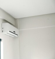 Aparelho de ar condicionado branco fixado em parede em um quarto com paredes lisas.