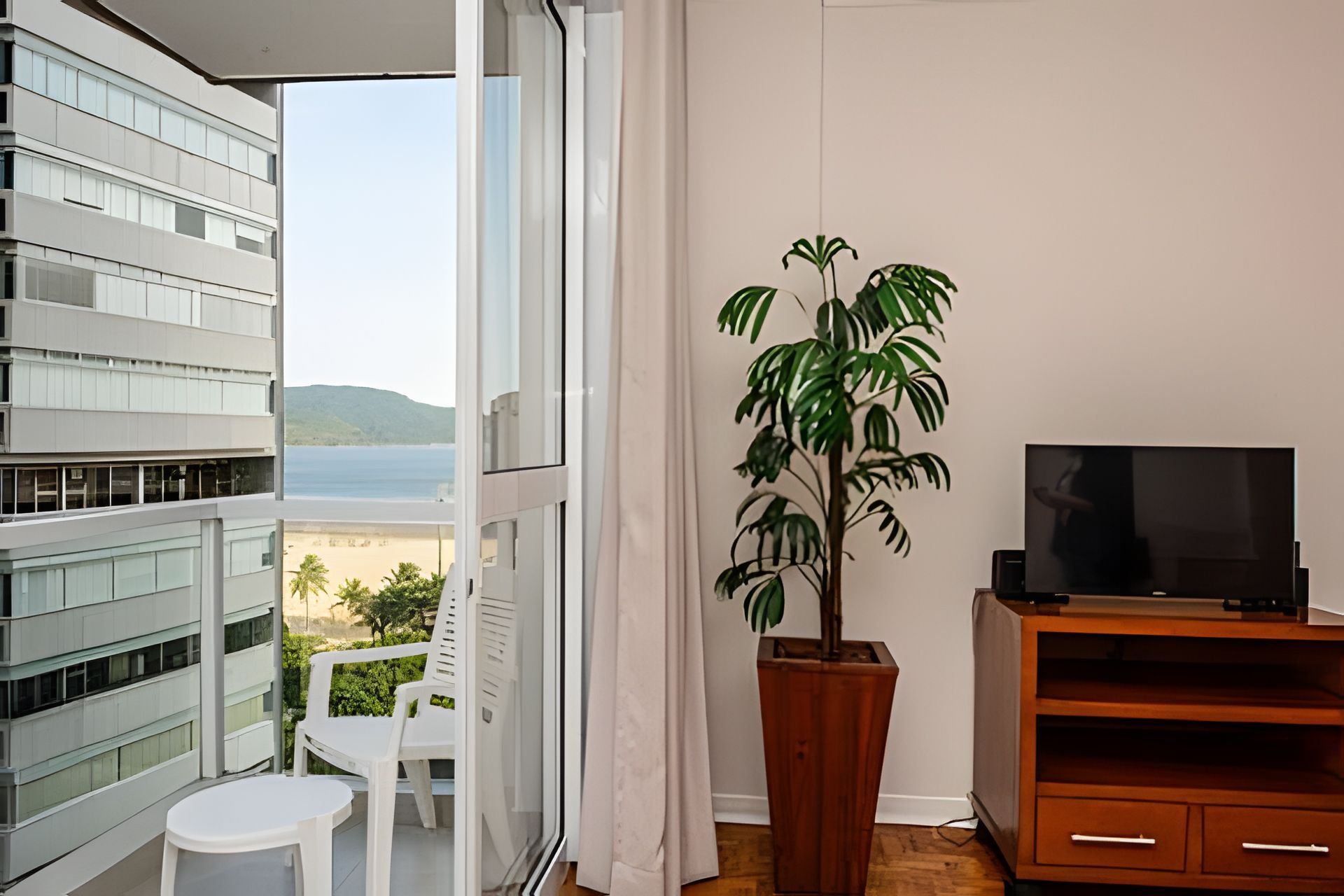 Varanda com vista para o mar, um vaso de planta, uma cadeira branca e um móvel de entretenimento de madeira.