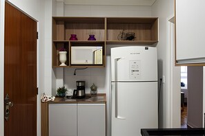 Uma cozinha compacta com uma geladeira branca, micro-ondas e cafeteira no balcão.