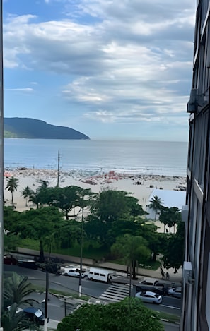Vista costeira com uma praia, estrada com carros estacionados e um edifício em primeiro plano.