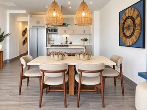 Uma sala de jantar moderna com uma mesa retangular, seis cadeiras e duas luminárias pendentes.
