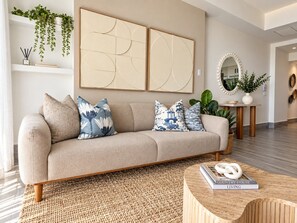 Uma sala de estar moderna com um sofá bege, almofadas decorativas, uma mesa de centro redonda com livros e um grande quadro abstrato na parede.