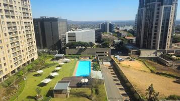 Um edifício alto com piscina no terraço e áreas verdes ao redor.