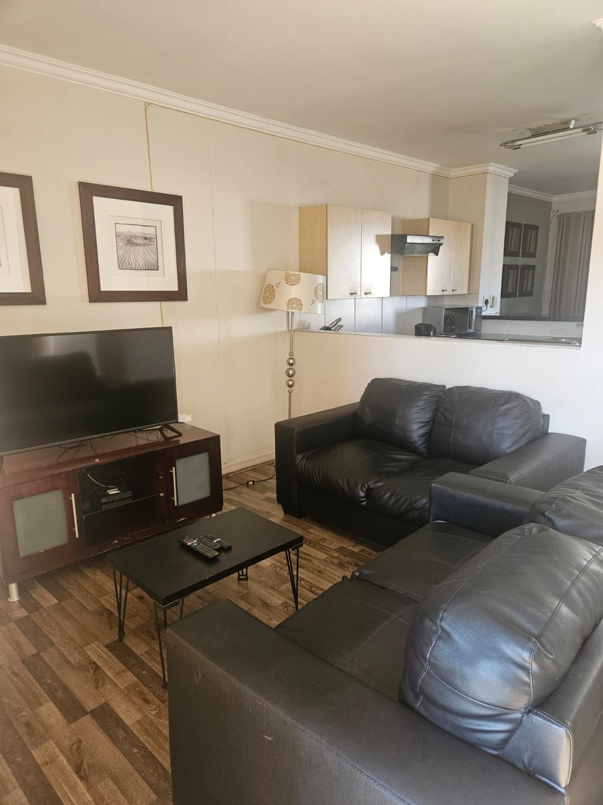 Uma sala de estar com televisão de tela plana, sofá, mesa de centro e abajur.