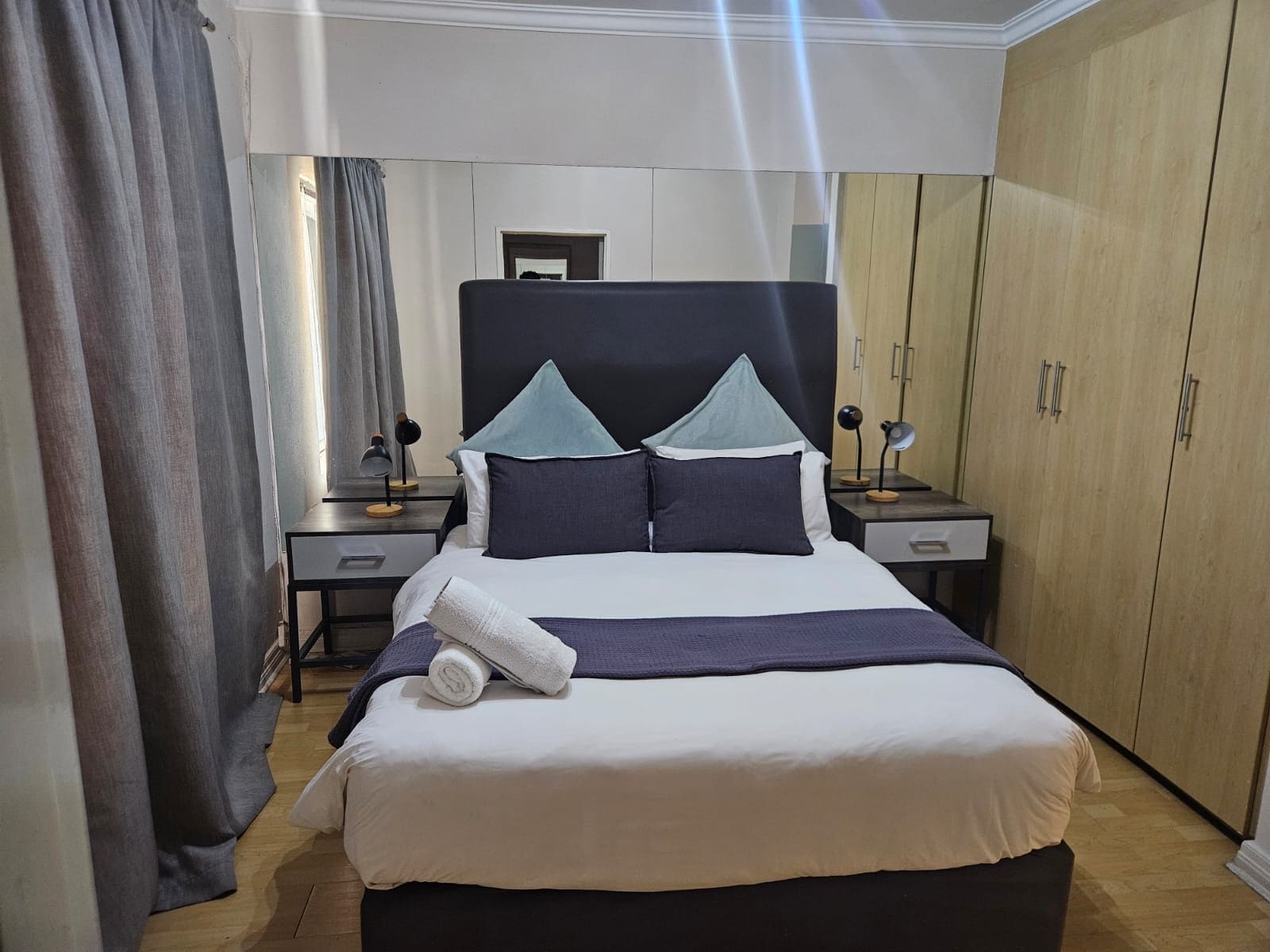 Quarto de hotel com cama, duas mesas de cabeceira, um guarda-roupa e uma cortina.