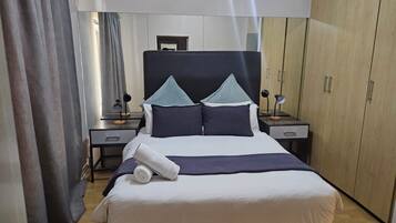 Quarto de hotel com cama, duas mesas de cabeceira, um guarda-roupa e uma cortina.