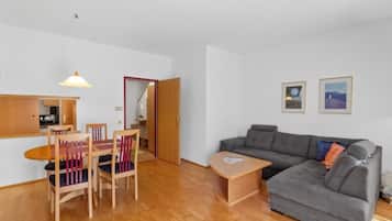 Sala de estar com sofá cinza, mesa de jantar de madeira com cadeiras, pequena mesinha de madeira e luminária pendente.