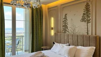 Quarto de hotel com cama grande, um lustre, vista através de uma porta de vidro e parede com desenho de árvore.