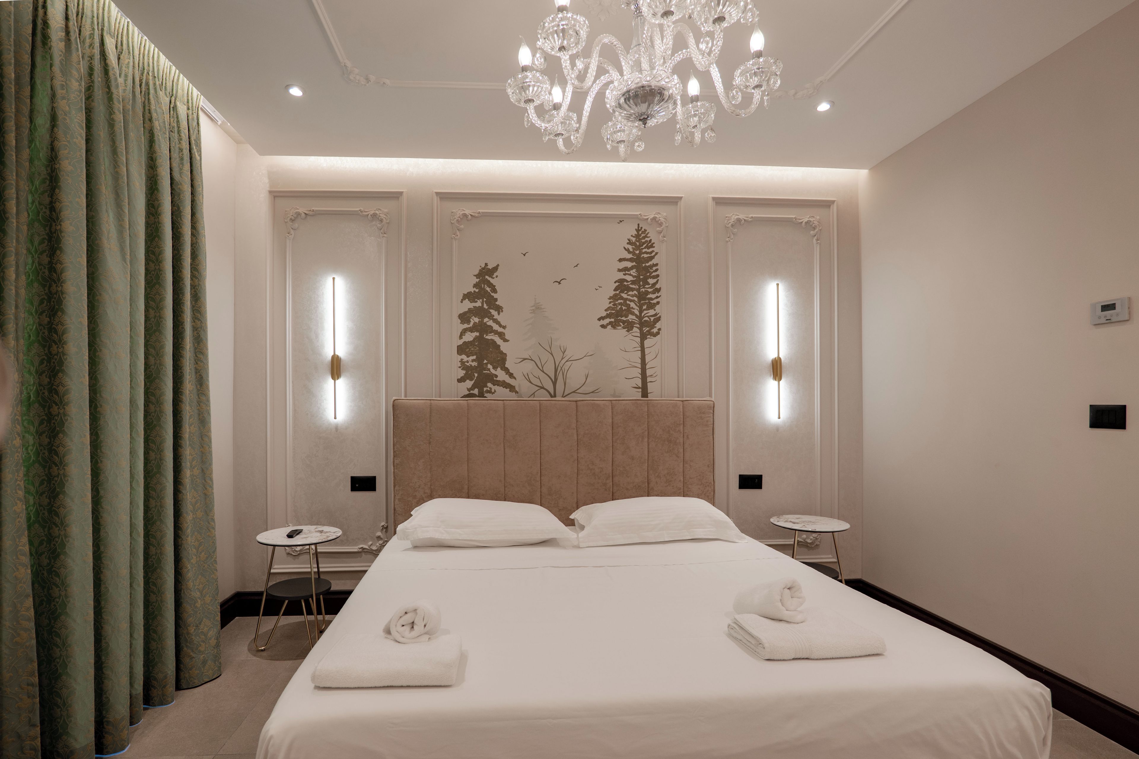 Quarto de hotel com uma cama grande, duas mesas de cabeceira, um candelabro e uma parede com um mural de tema natural.