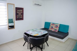 Uma sala de estar compacta com sofá, mesa redonda e cadeiras, espelho e um cartaz motivacional na parede.