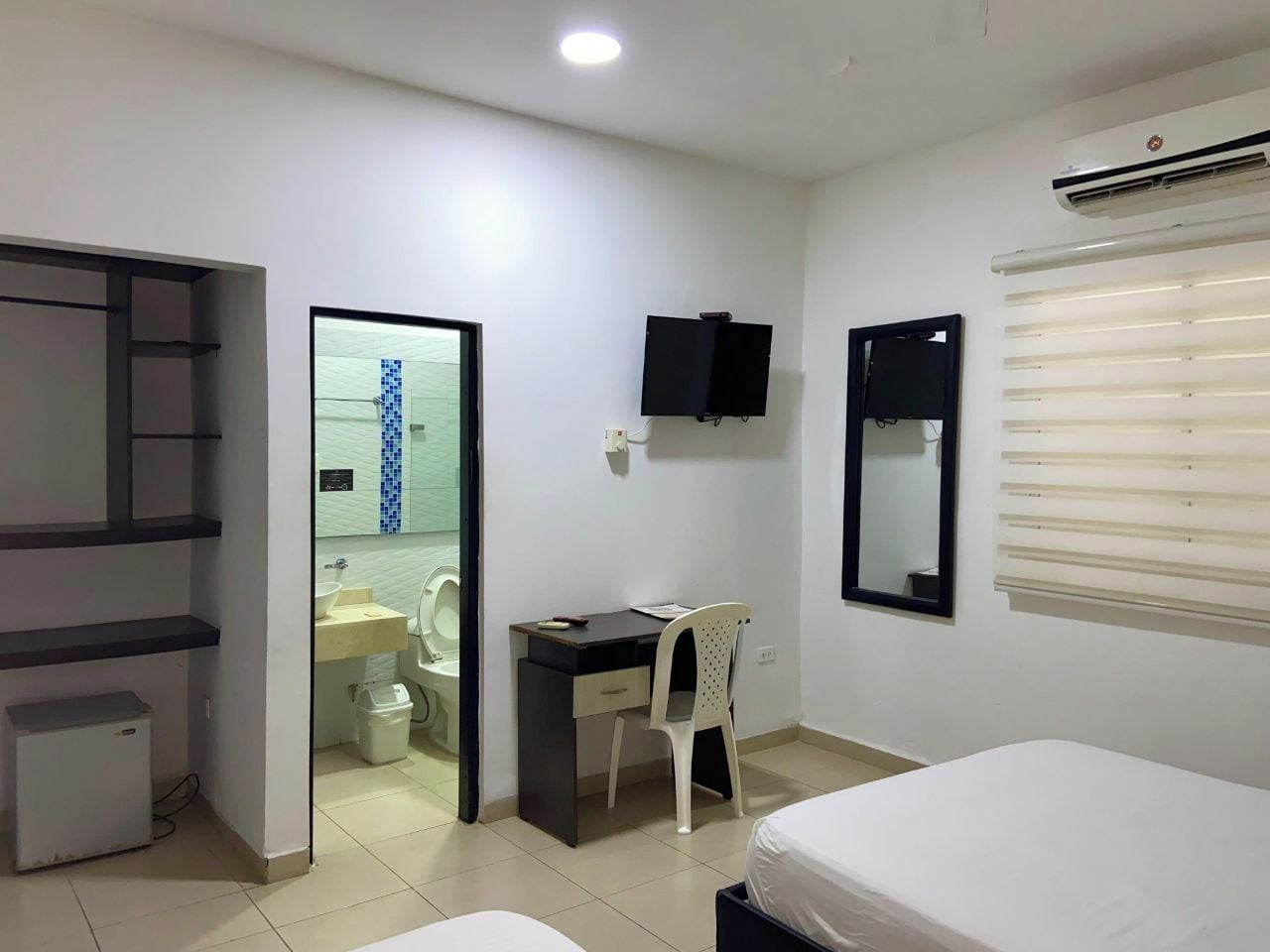 Quarto de hotel com cama, escrivaninha, cadeira, televisão e banheiro.