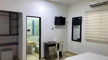 Quarto de hotel com cama, escrivaninha, cadeira, televisão e banheiro.