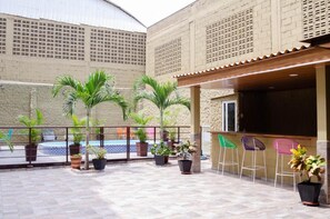 Área de varanda externa com piscina, plantas em vasos e banquetas de bar.