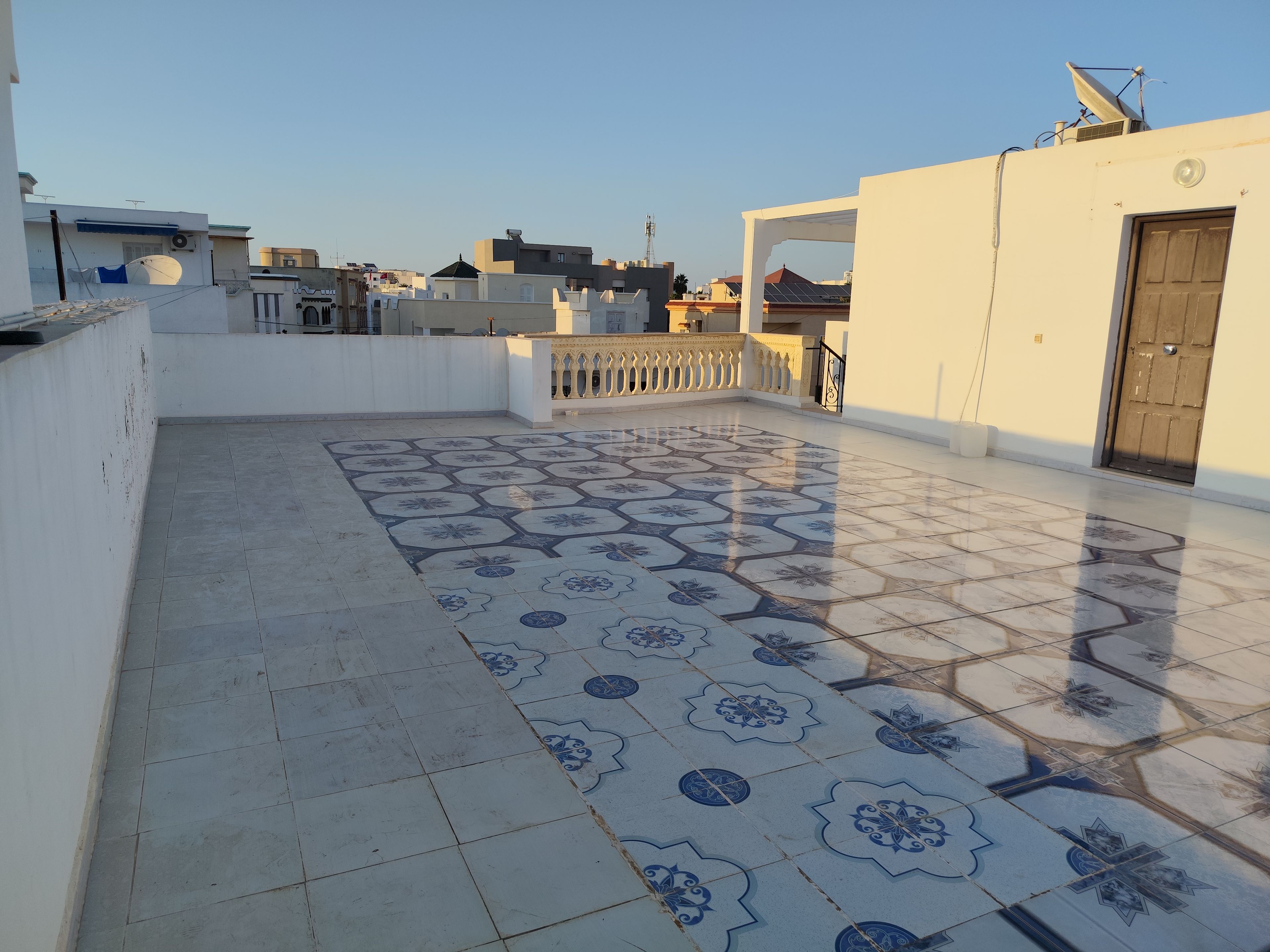Terraço no telhado com azulejos estampados, uma parede branca e uma porta.