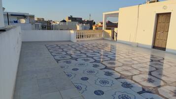Terraço no telhado com azulejos estampados, uma parede branca e uma porta.