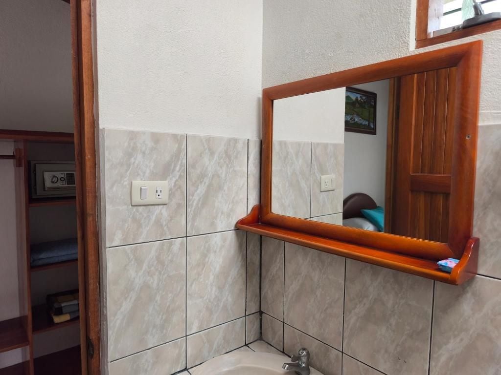 Casa de banho com parede de mármore, espelho com moldura de madeira e lavatório branco.