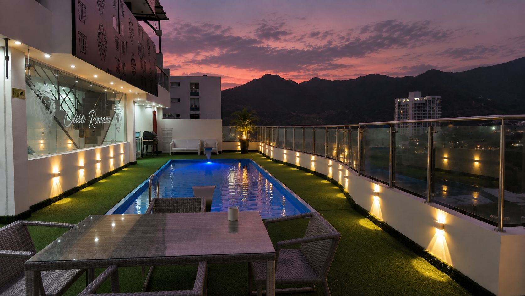 Área de piscina no terraço, com guarda-corpo de vidro, mesa de jantar e cadeiras.