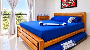 Quarto de hotel com cama, mesa de cabeceira, janela com cortinas e vista para palmeiras.