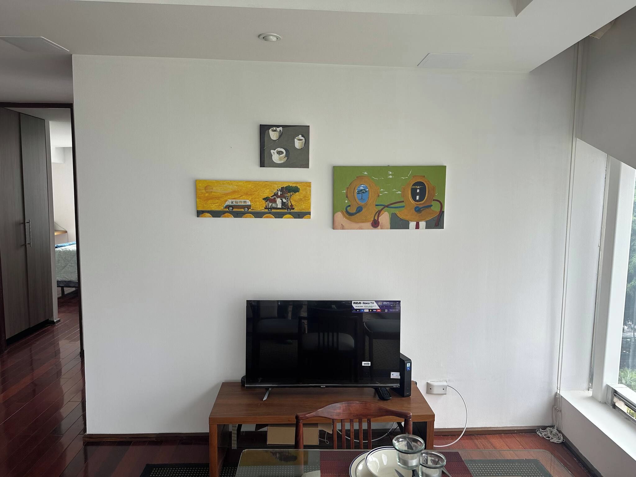 Sala de estar com televisão de tela plana, mesa de centro de madeira e duas pinturas na parede.