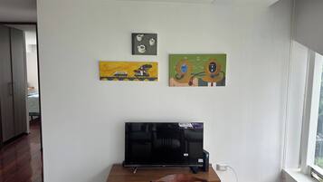 Sala de estar com televisão de tela plana, mesa de centro de madeira e duas pinturas na parede.