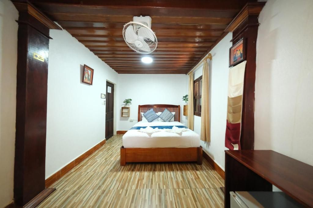 Quarto de hotel com teto de madeira, cama com estrutura de madeira, mesa de cabeceira e ventoinha fixada na parede.