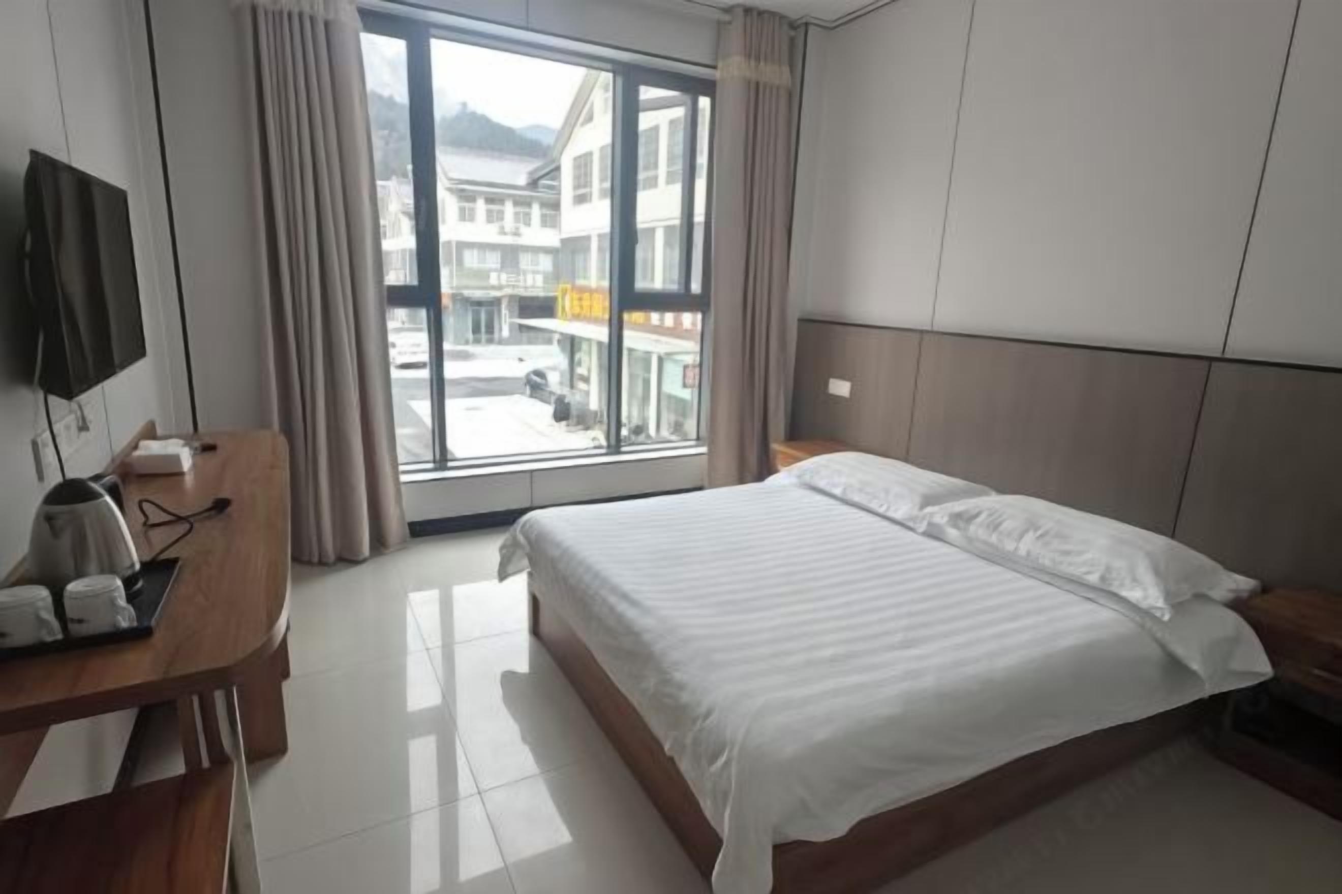 Quarto de hotel com cama, escrivaninha, televisão e janela com cortinas.