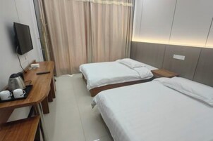Quarto de hotel com duas camas, uma mesa de trabalho com cafeteira, televisão e cortina.