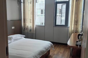 Quarto de hotel com cama, escrivaninha, cadeira, janela e cortinas.