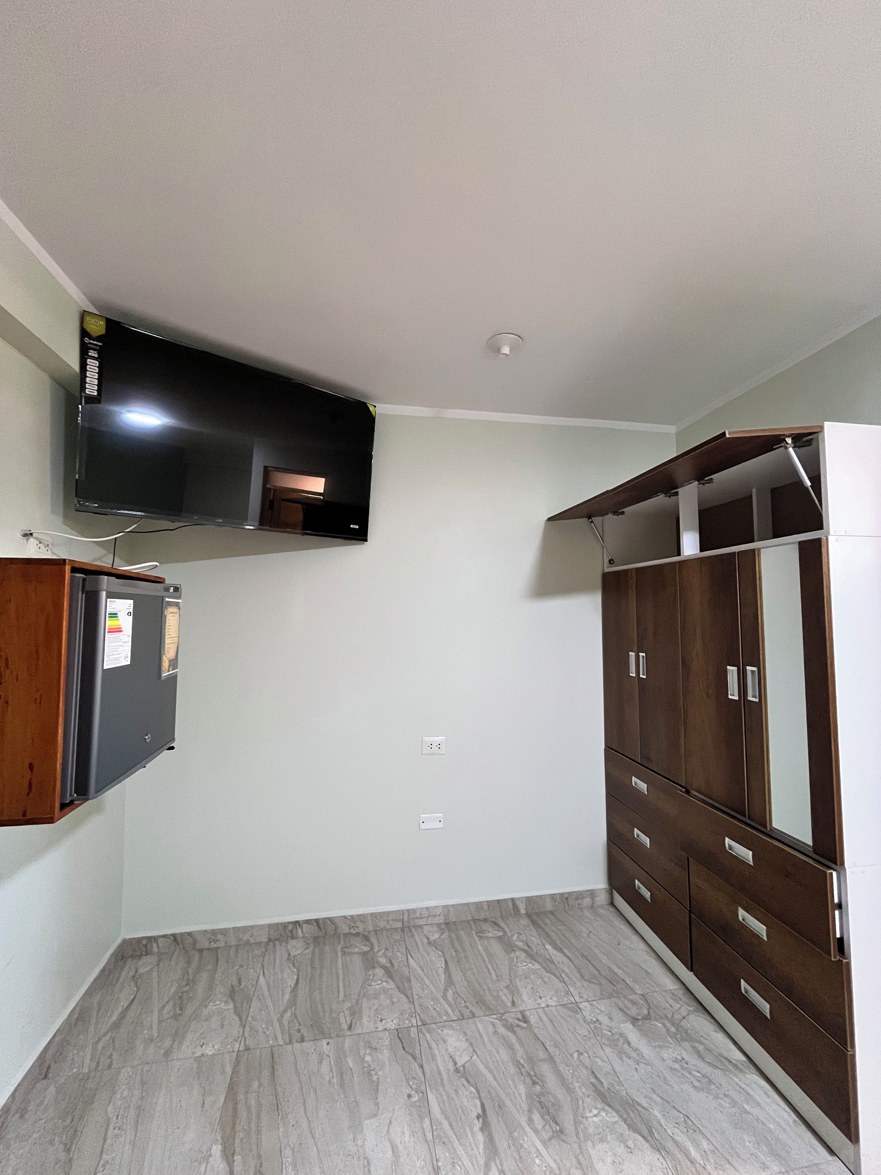 Quarto com televisão de tela plana na parede, armário embutido com várias gavetas e piso em azulejos.