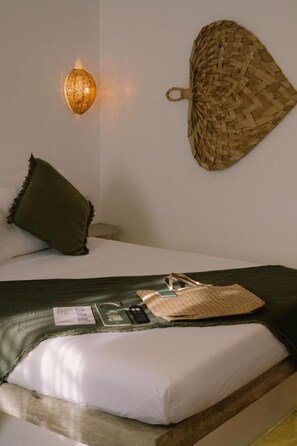 Uma cama com um cobertor verde, uma cesta de palha e um luminário fixado na parede.